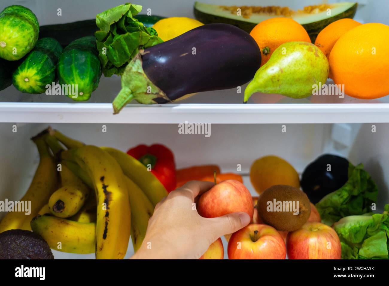 Hand picking up an apple from a fridge full of healthy food with fruits ...