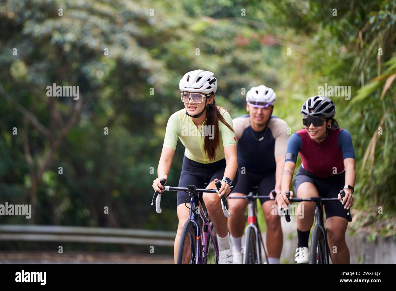 group of three young asian adult cyclists riding bike on rural road ...