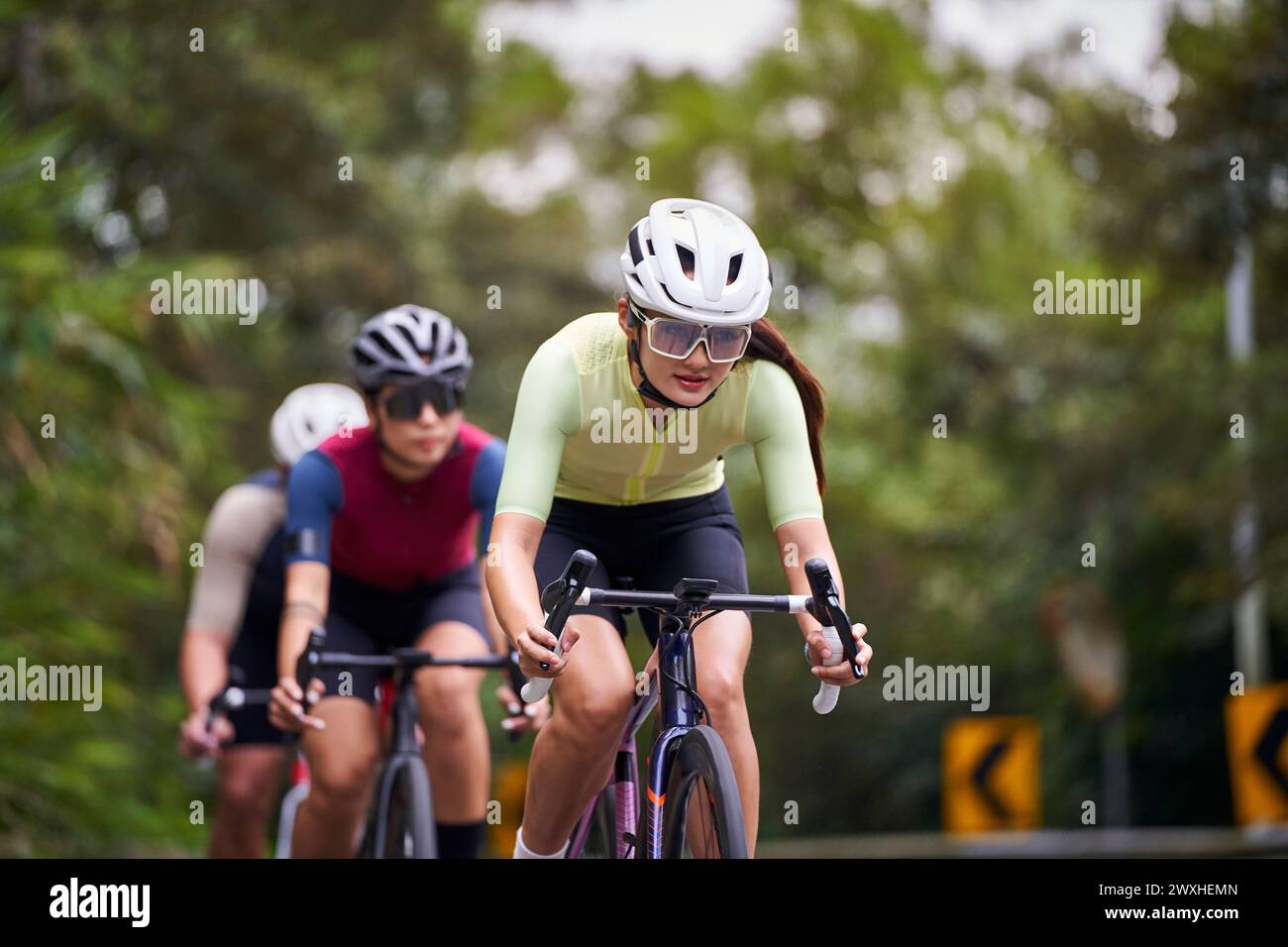 group of three young asian adult cyclists riding bike on rural road ...