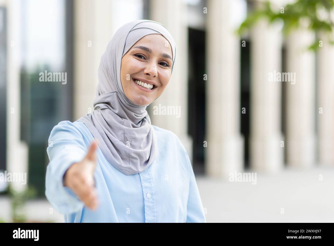 A cheerful Muslim woman wearing a hijab extends a handshake ...