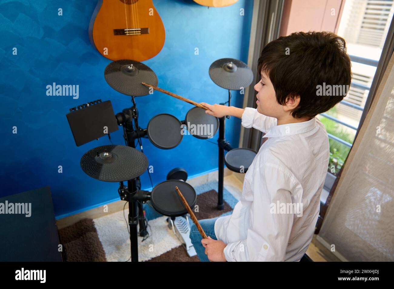 Overhead rear view of a Hispanic teenager boy musician using drumsticks ...