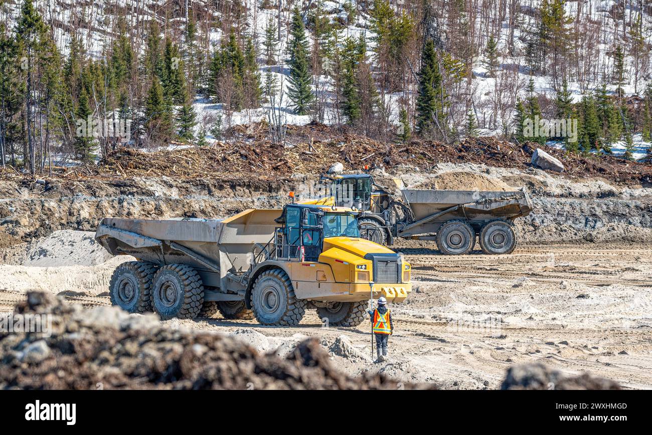 Two dump trucks transporting sand to a construction site, with a ...