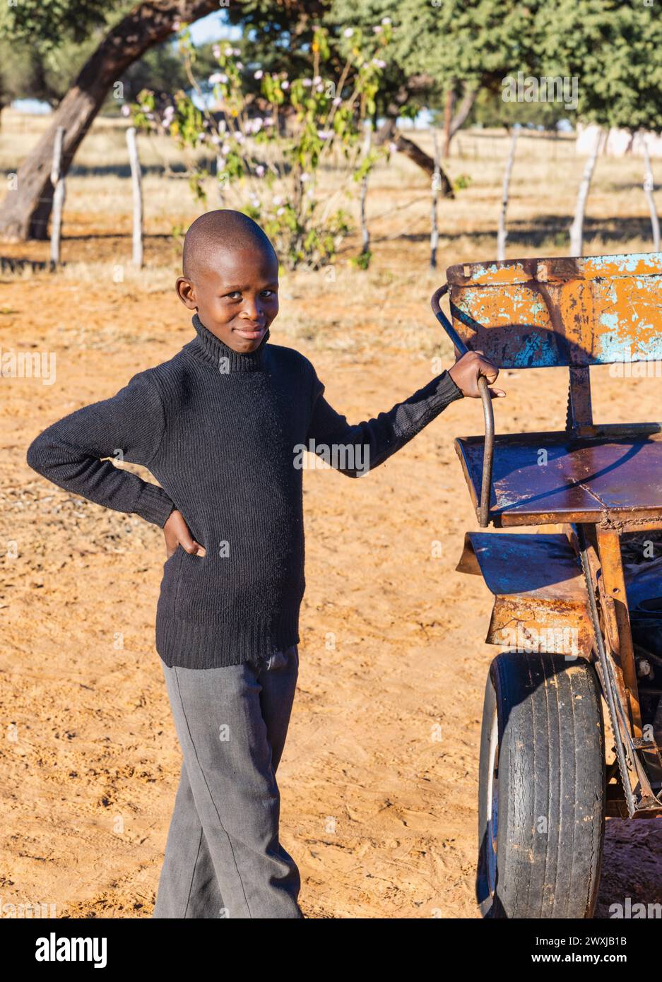 smiling african child standing next to a rusty donkey cart in the ...