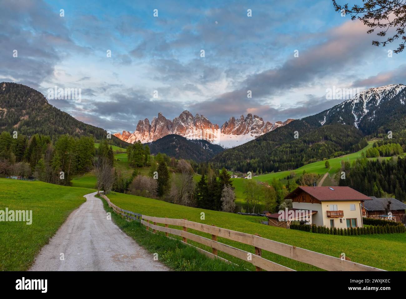 Village road in Alpine meadow and buildings against the Geisler ...
