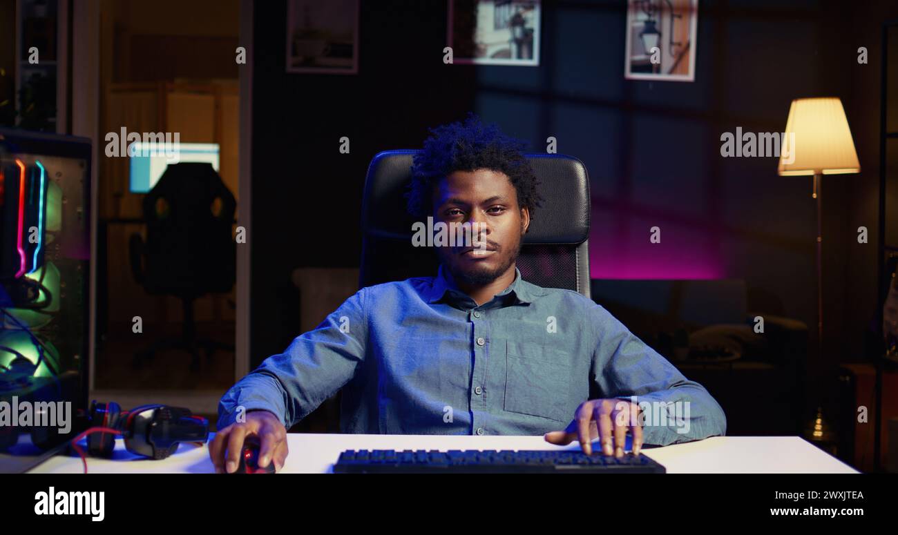 BIPOC man playing game on rgb lit computer desktop late at night ...