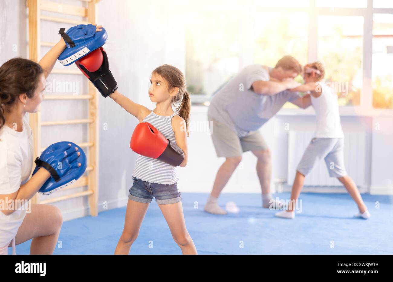 Girl and mom are boxing in gym, mother helps child to work out force of ...