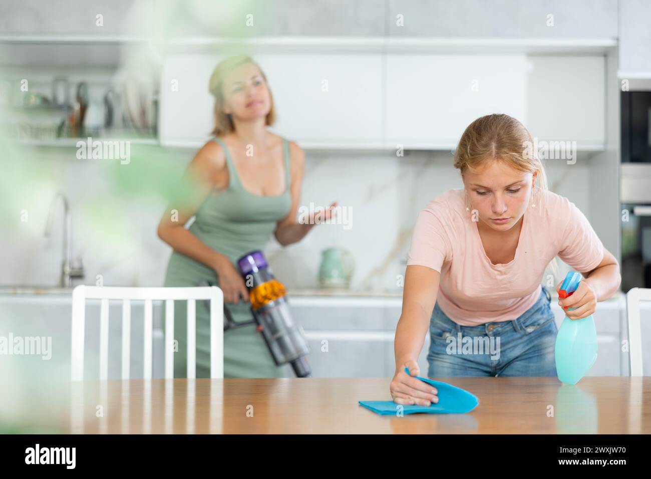 Teenage girl assisting mother in cleaning apartment, wiping kitchen ...