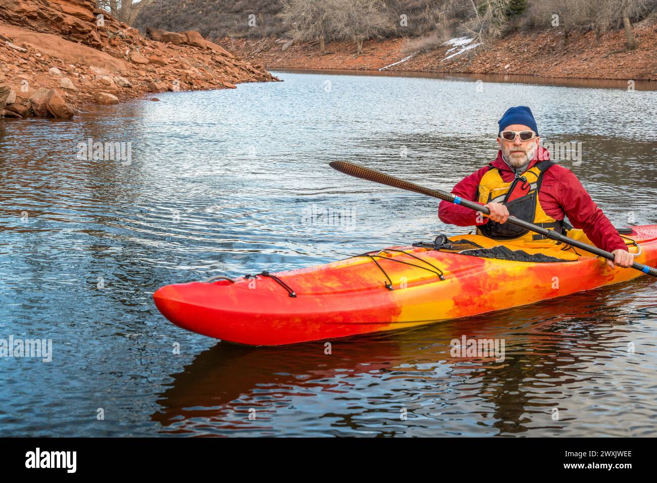 senior male paddler is paddling colorful river kayak on a calm lake ...