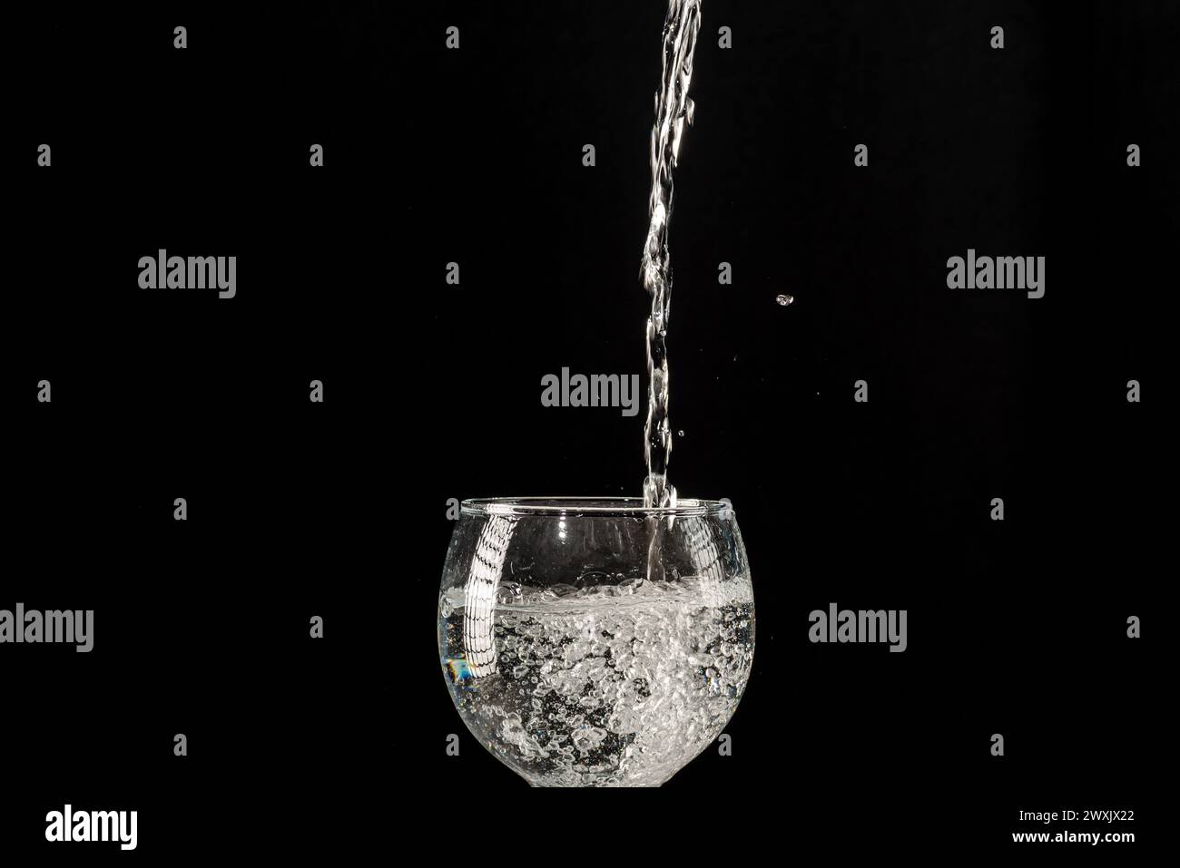 Water falling from above into a wine glass. Isolated on black ...
