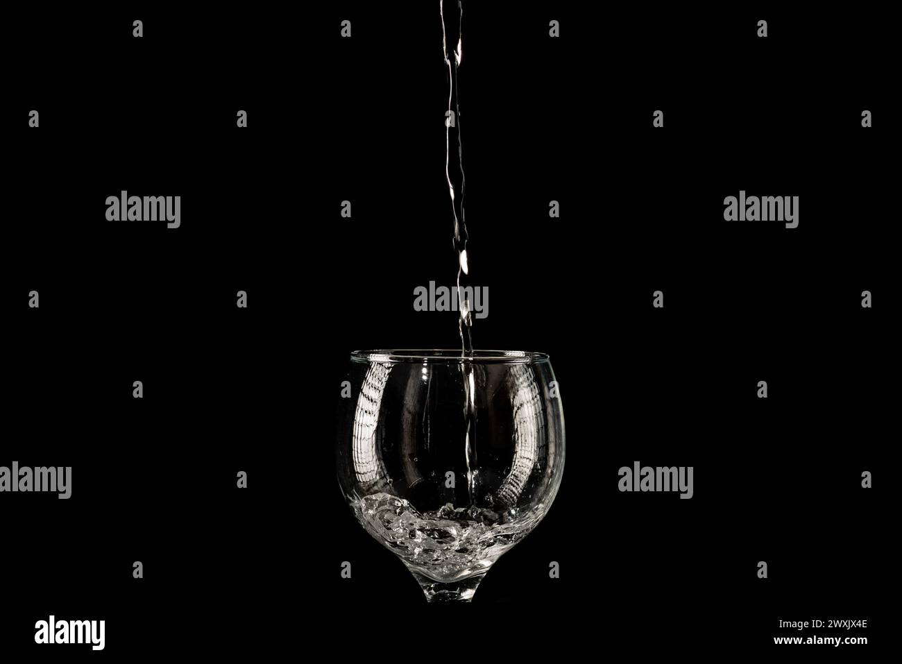 Stream of water in drops falling into a glass cup against a black ...