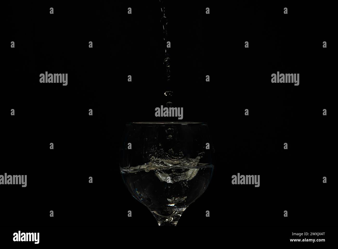 Water falling from above into a wine glass. Isolated on black ...