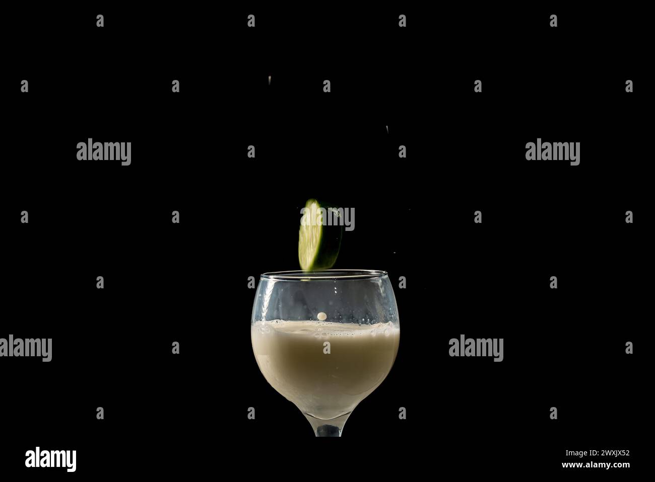 A slice of lemon falling into a glass cup with milk inside. Isolated on ...