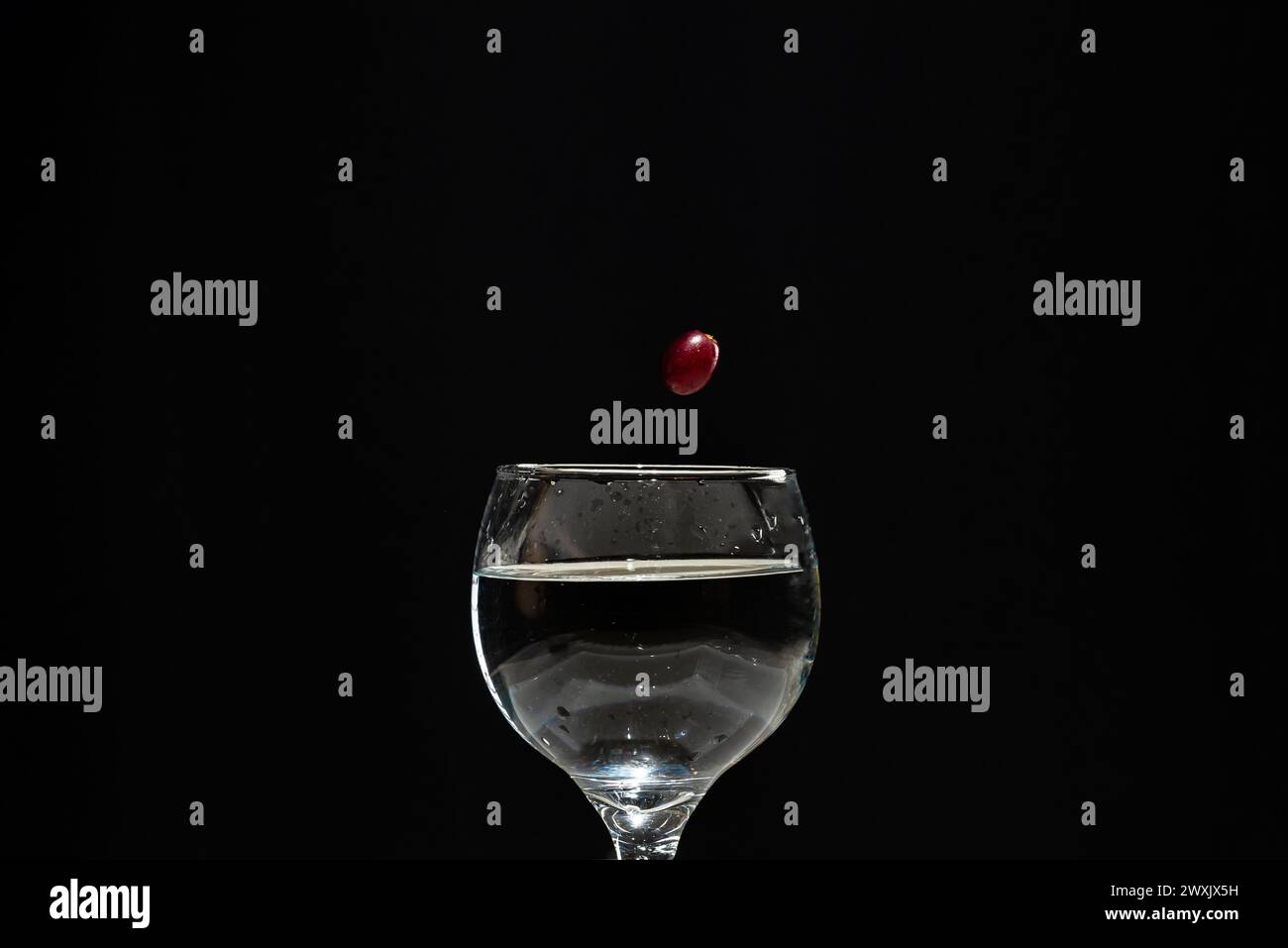 Grape falling from above into a wine glass. Isolated on black ...