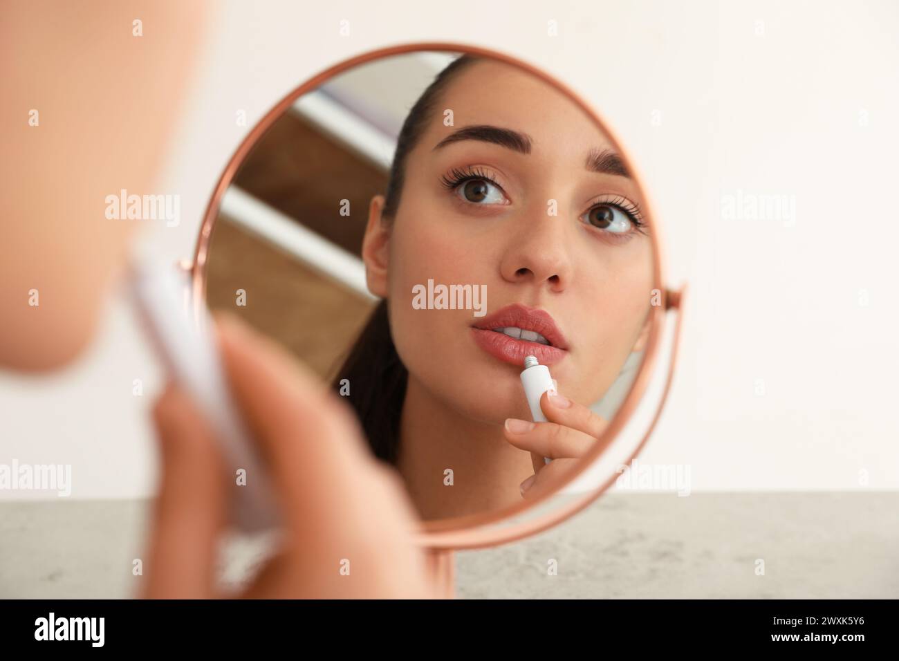 Woman with herpes applying cream on lips in front of mirror against ...
