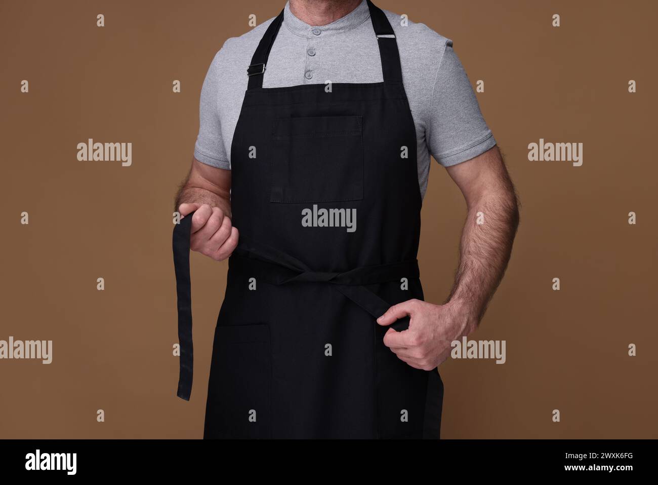 Man wearing kitchen apron on brown background, closeup. Mockup for ...