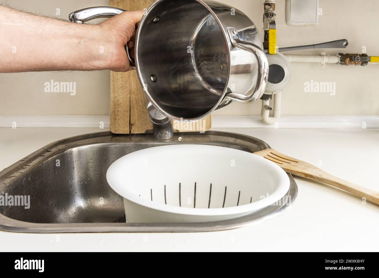 Emptying water from a pot onto a drainer in a kitchen sink Stock Photo ...