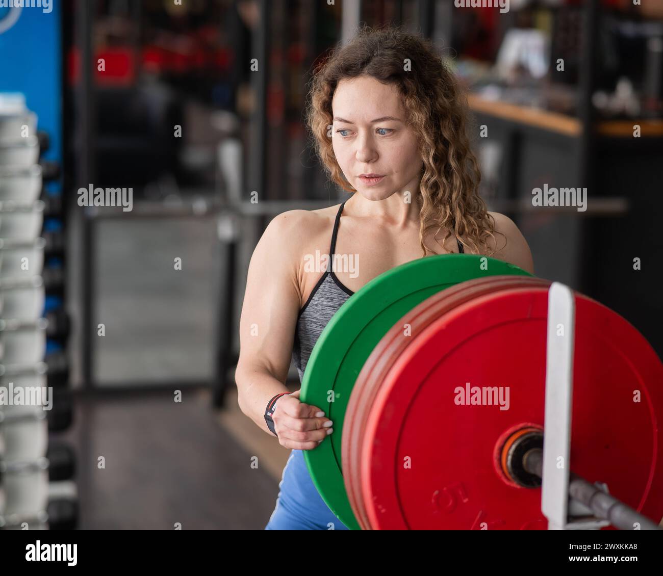 Caucasian forty year old woman putting a weight plate on a barbell in ...