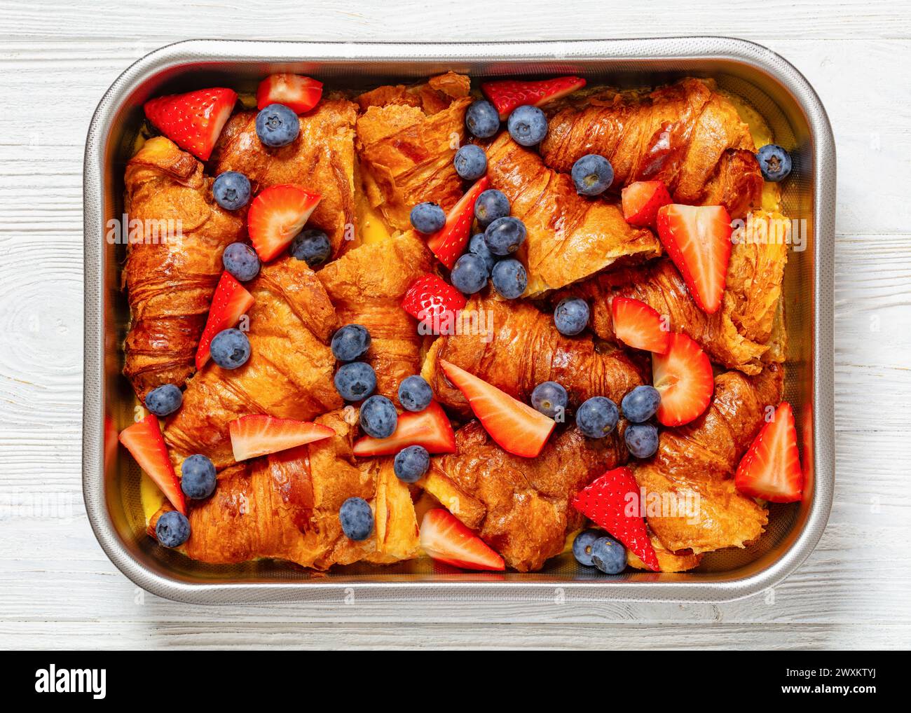 strawberry blueberry croissant casserole in baking dish on white wooden ...