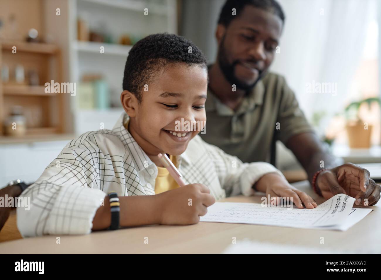 Portrait of smiling Black boy doing homework at kitchen table with ...