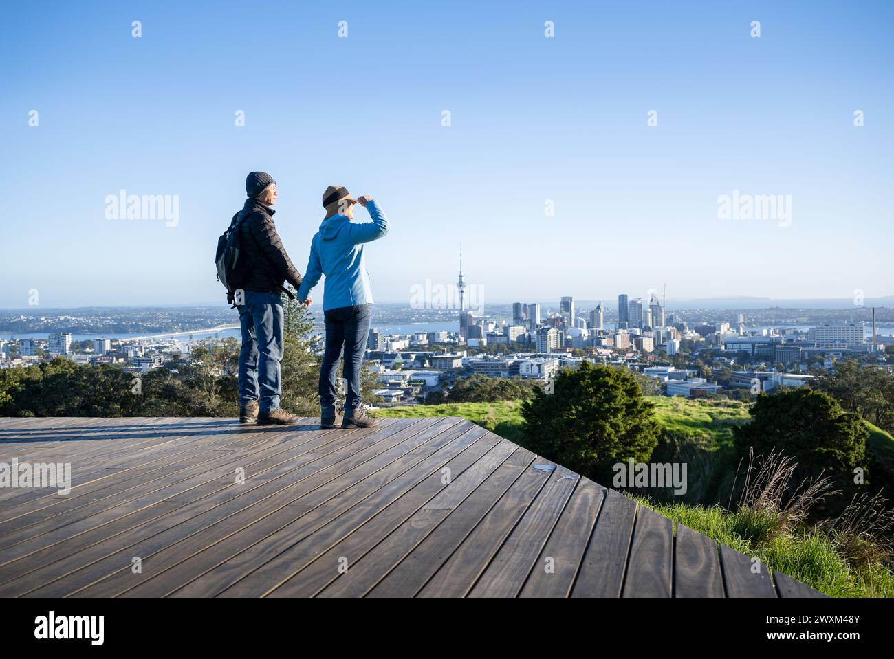 Couple standing on boardwalk at Mt Eden summit. Sky Tower and Auckland ...