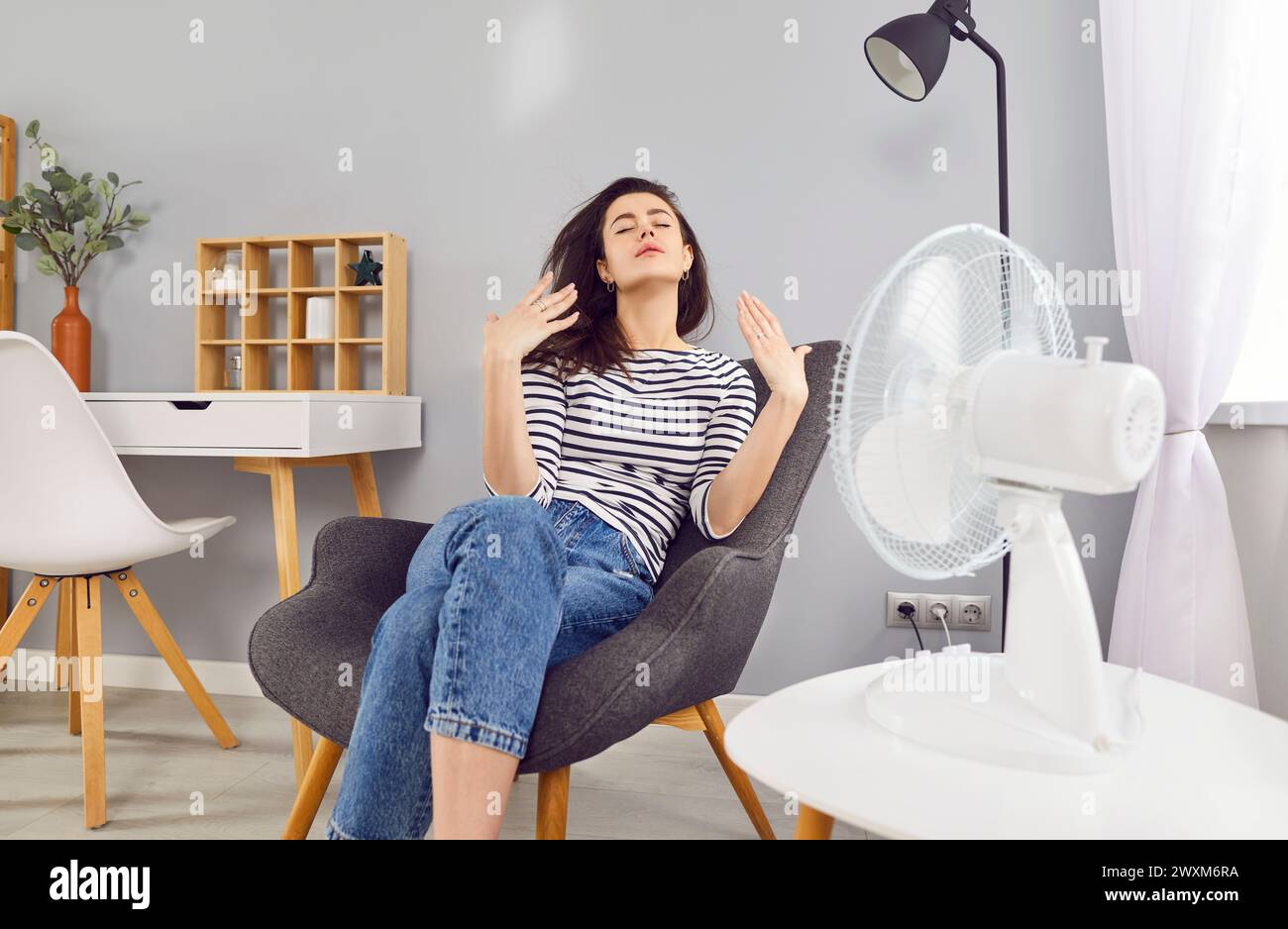 Young woman, exhausted from hot summer weather, sitting by an electric ...
