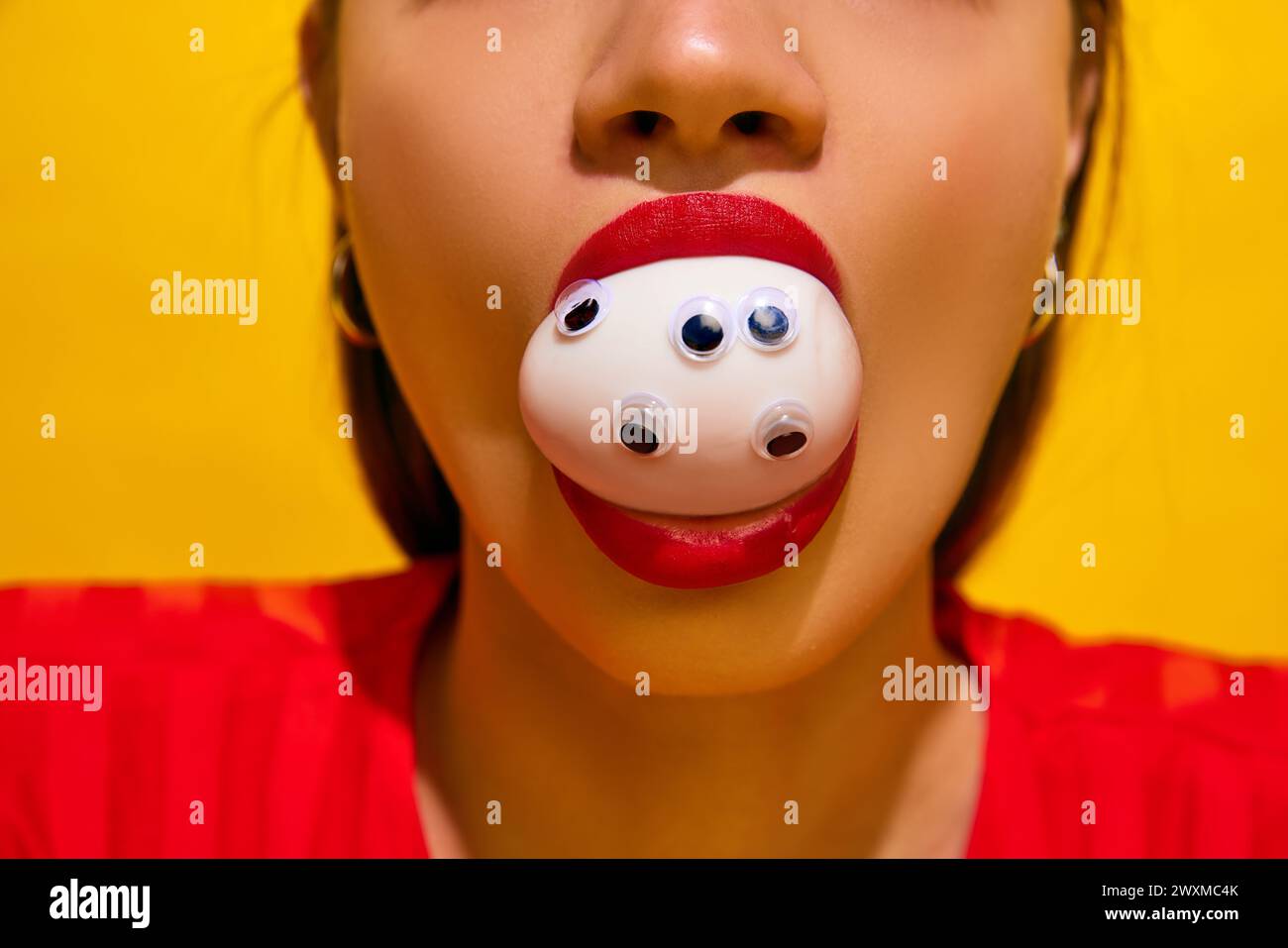 Close-up of woman's face with red lipstick, egg on mouth with googly ...