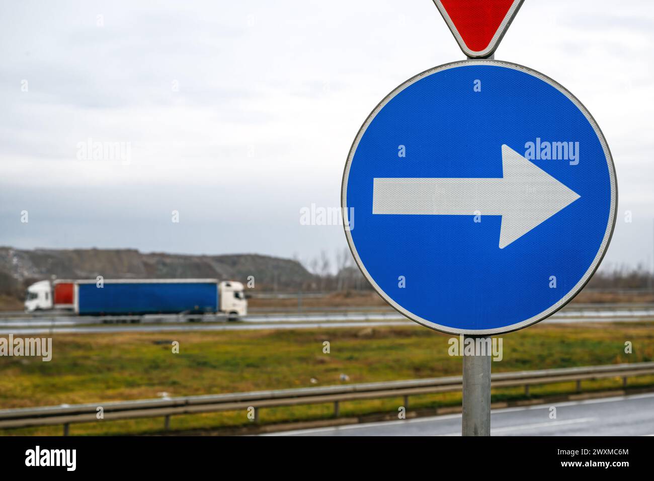 Mandatory direction arrow road sign on highway with two semi-trucks in ...