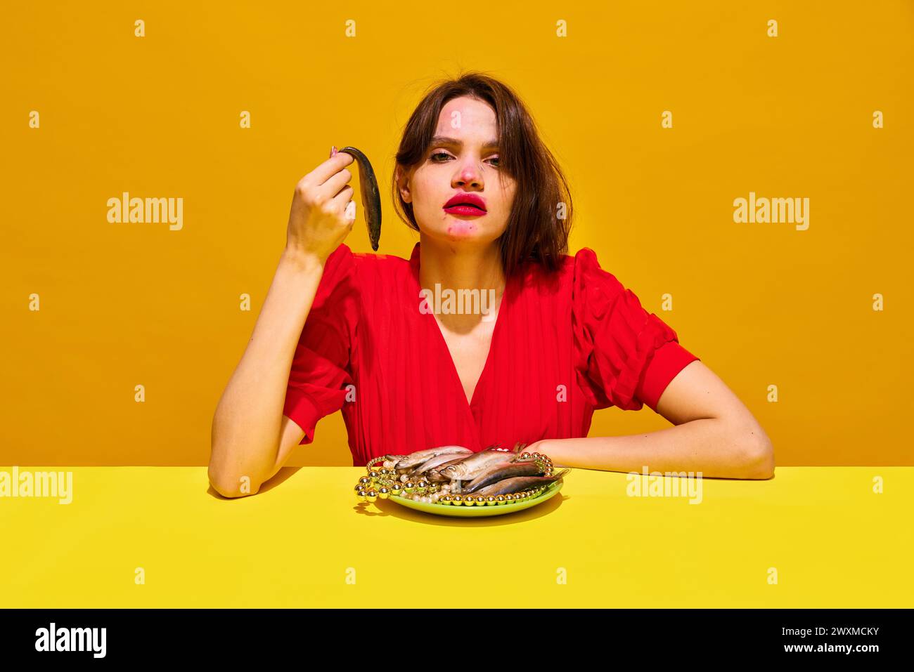 Young woman with smudged lipstick makeup eating fish against yellow ...