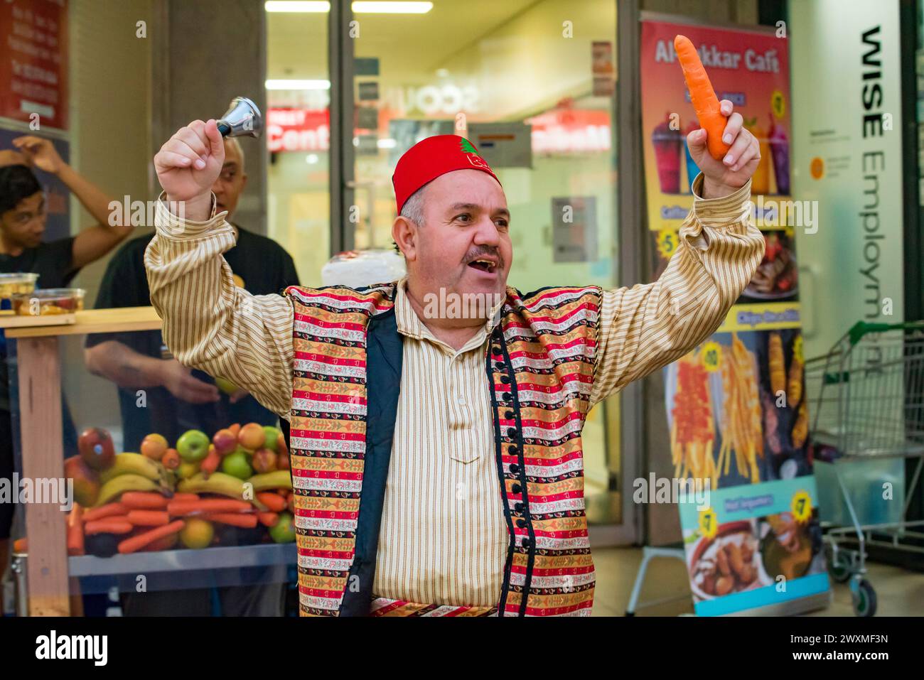 A happy man in a Fez shouting and ringing a bell at a street stall in ...