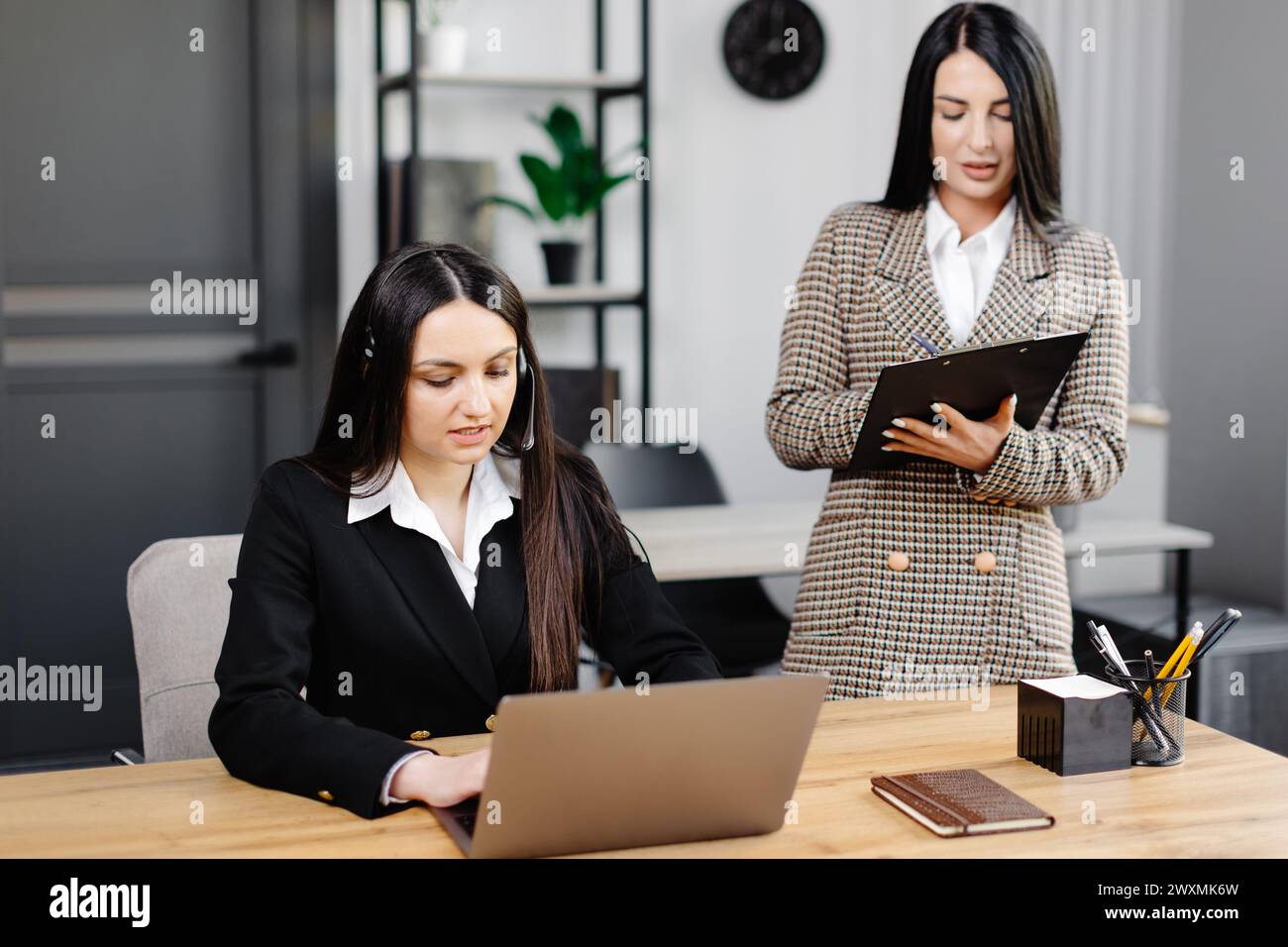 Call center agent with headset working on support hotline in modern office. Two young attractive ...