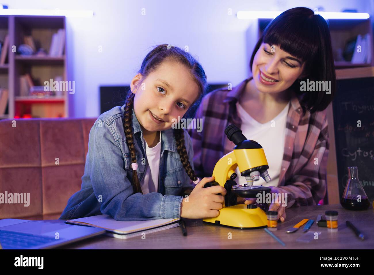 Focused little girl looking camera, working with electron microscope ...