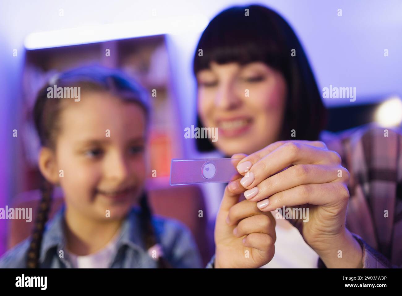 Young woman teaching girl to make biological research at evening home ...