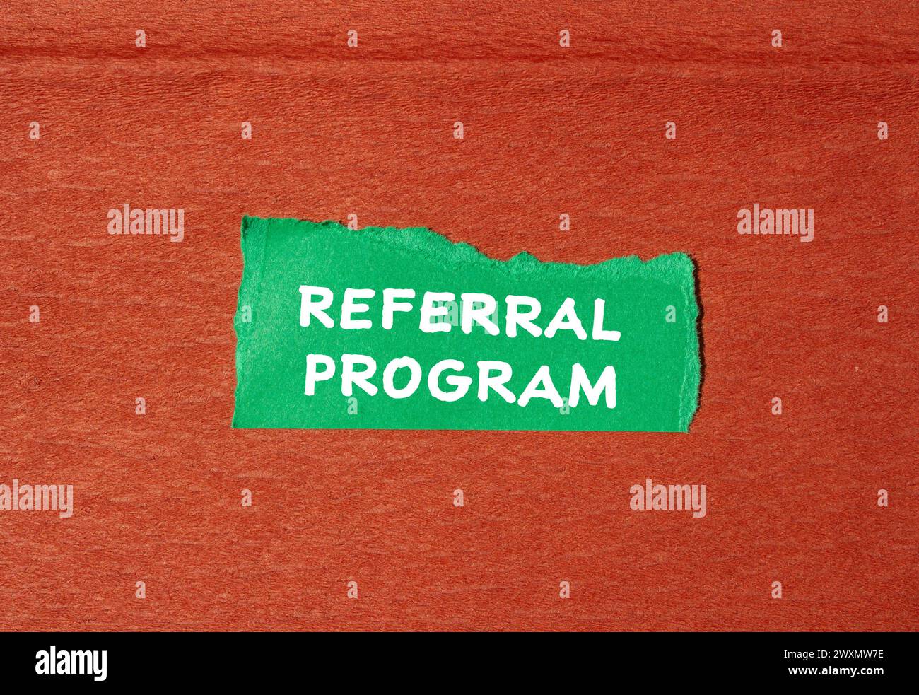 Referral program words written on green torn paper piece with brown background. Conceptual ...
