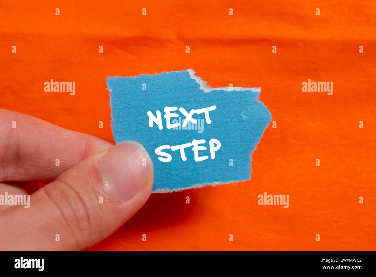 Next step words written on blue torn paper piece with orange background ...