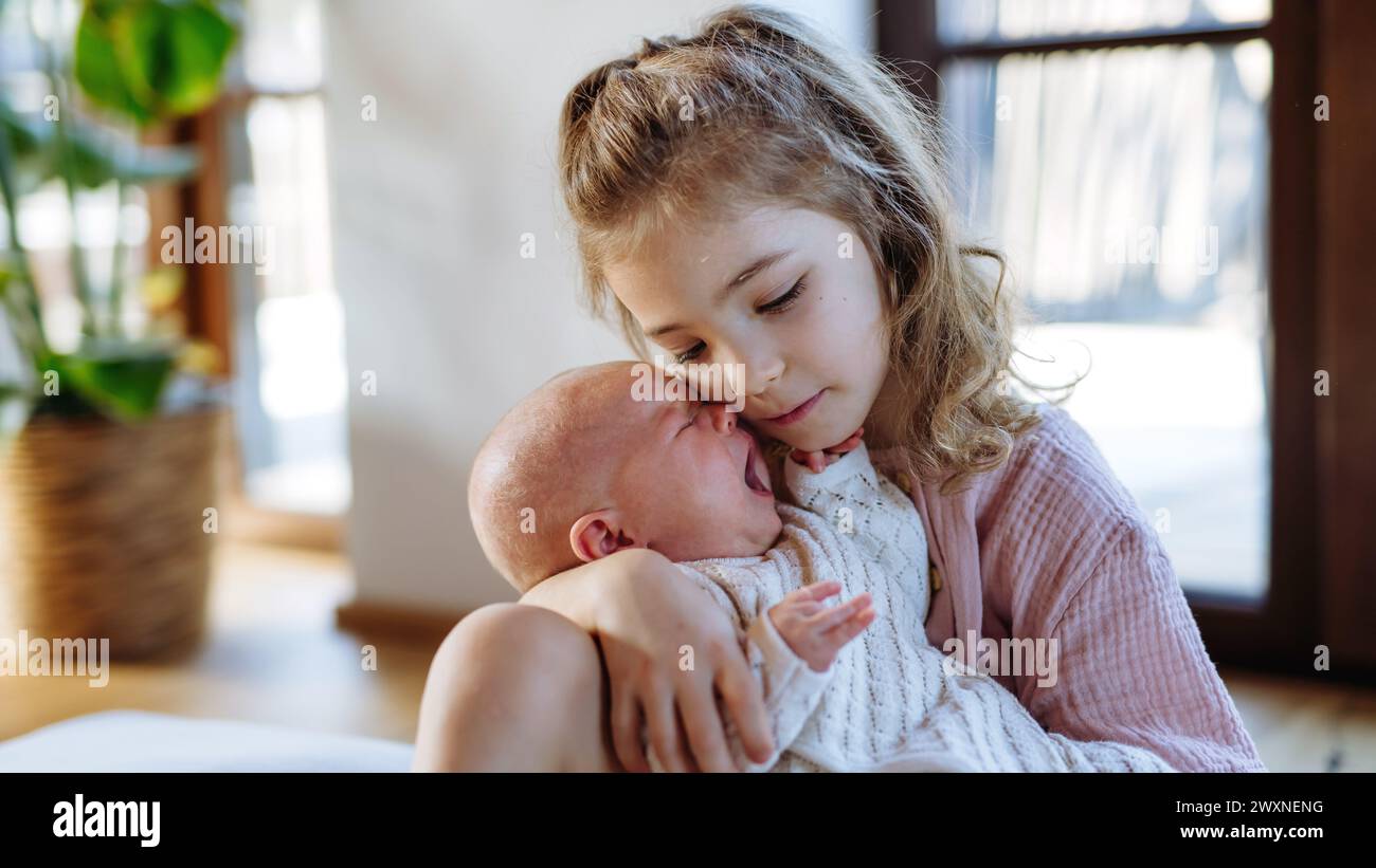 Portrait of big sister soothing newborn sister. Girl taking care of ...