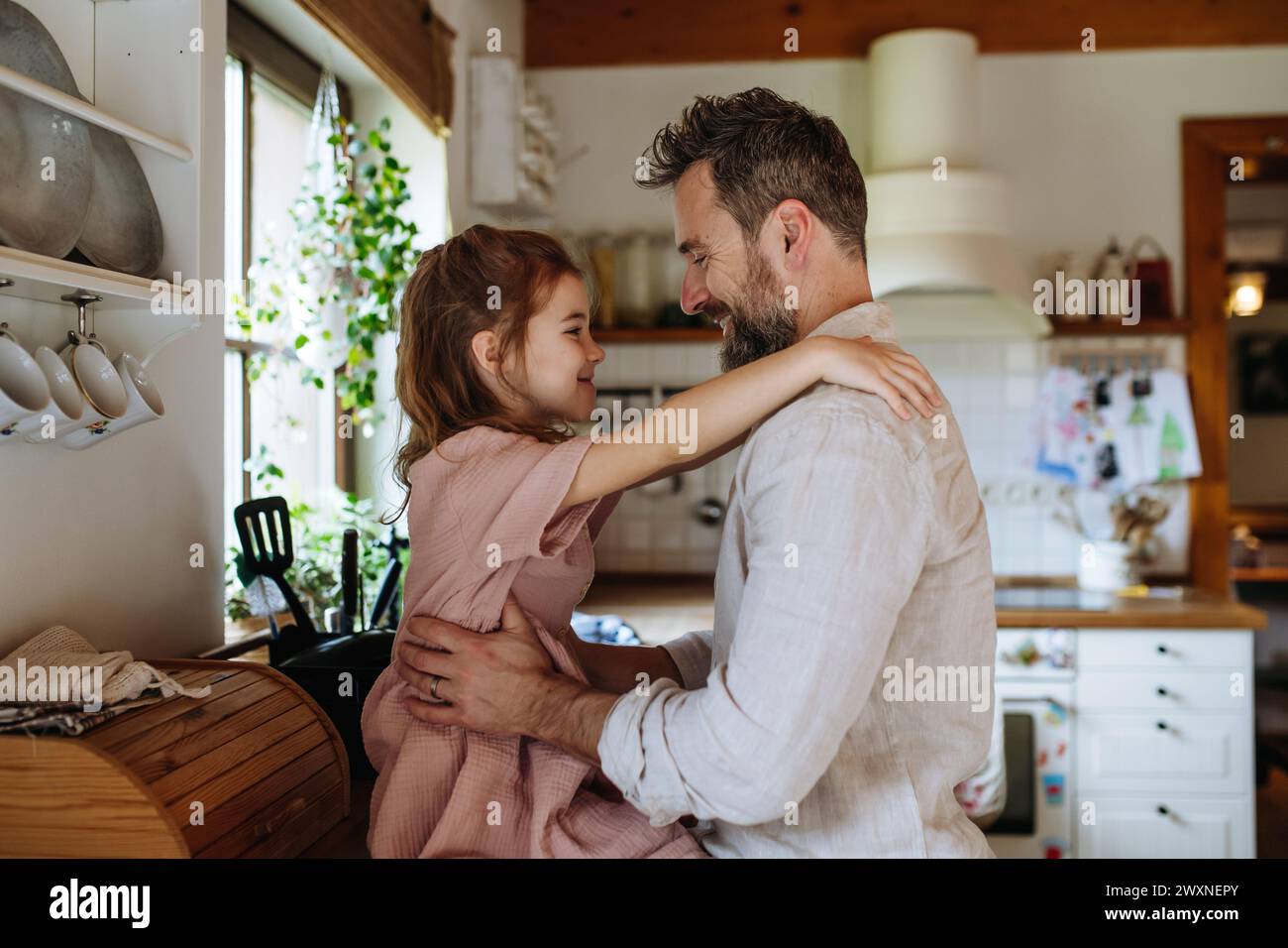 Daughter hugging father lovingly, sitting on kitchen counter ...