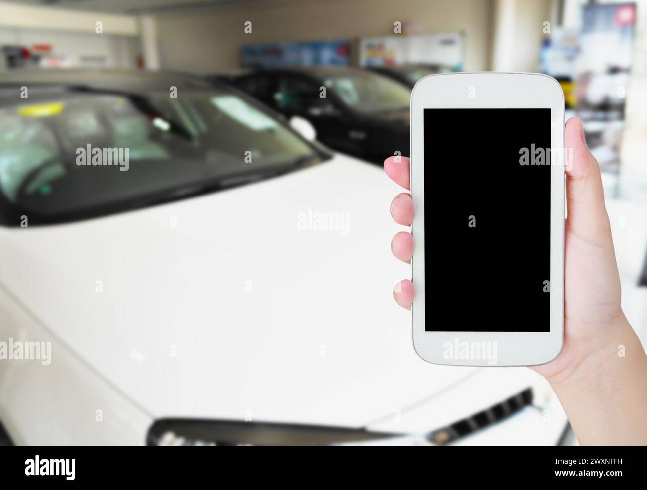 woman hands holding mobile phone with blurred background of new cars in ...