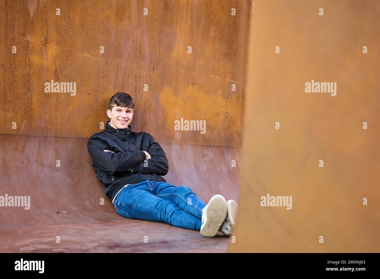 Young Man Sitting on Rusty Metal Structure, Sporting a Genuine Smile ...