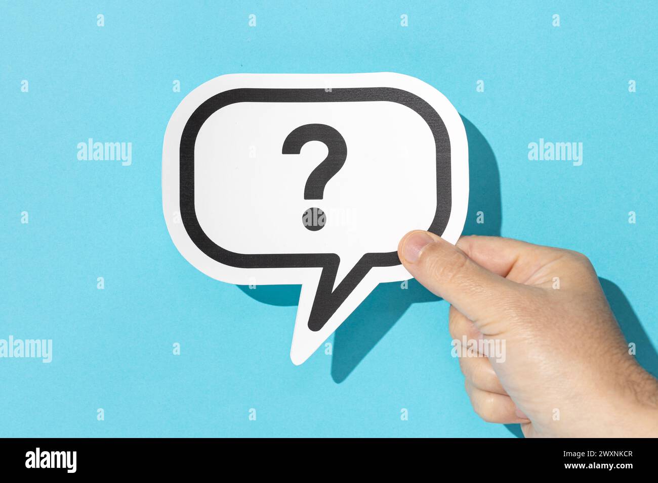 Hand holding a question mark on speech bubble on blue background. Doubt ...