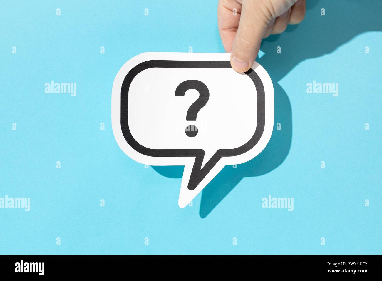 Hand holding a question mark on speech bubble on blue background. Doubt ...