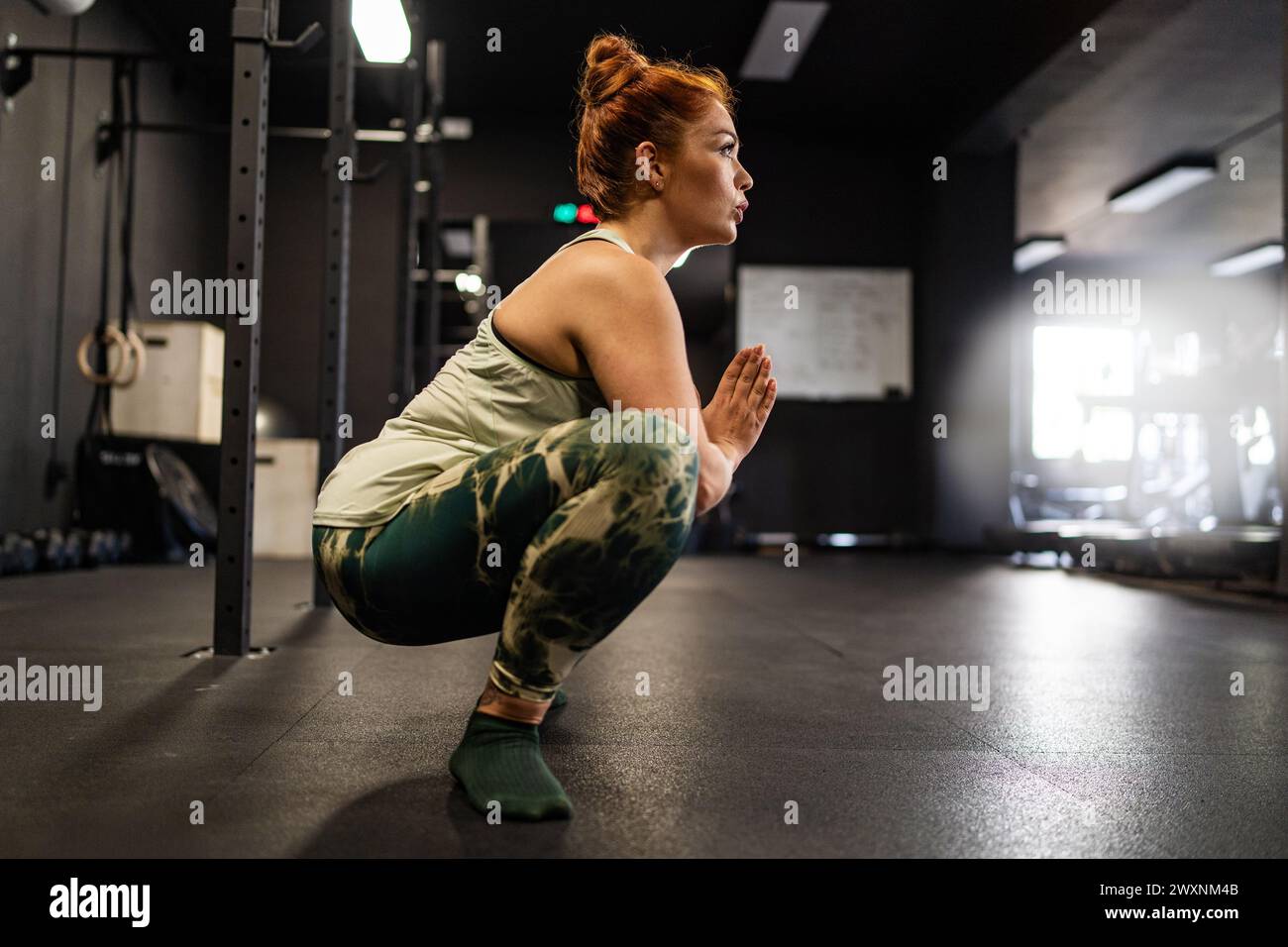 A focused woman perfecting a yoga squat in a gym setting, showcasing a ...