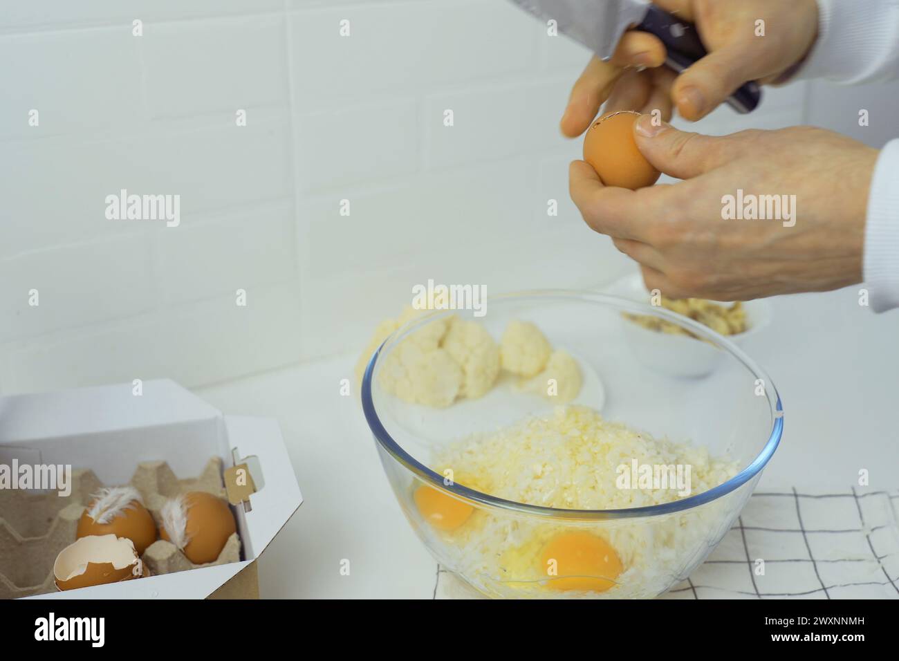 A man stands over a bowl of shredded cauliflower, cracking eggs and ...
