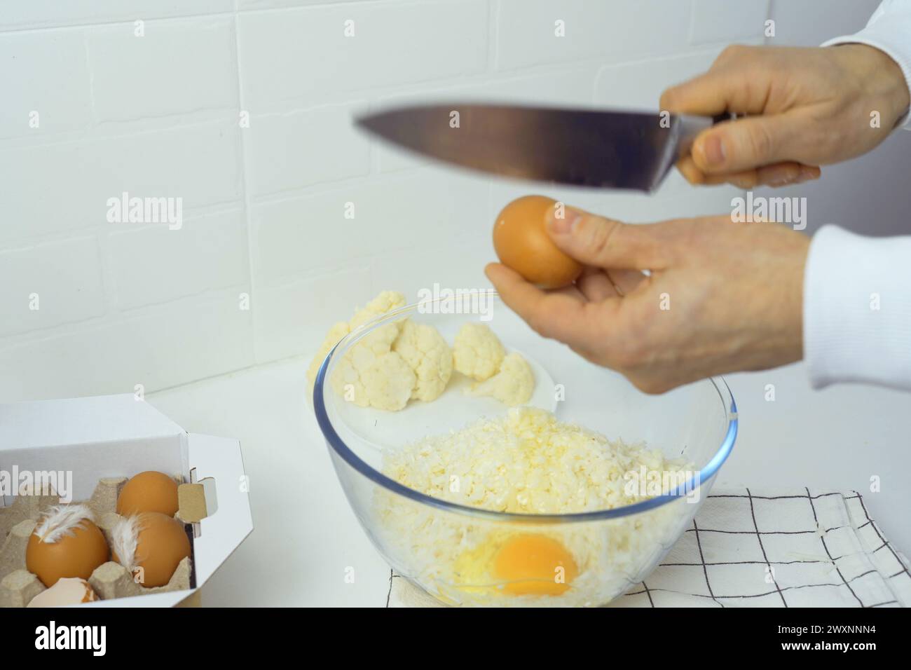 A man stands over a bowl of shredded cauliflower, cracking eggs and ...
