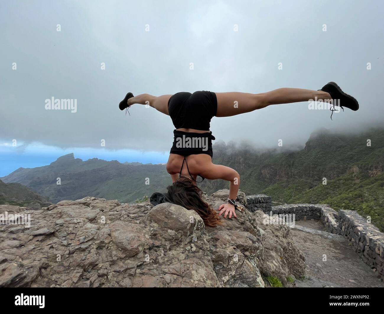 A person performing a handstand on a rock with scenic hills in the ...