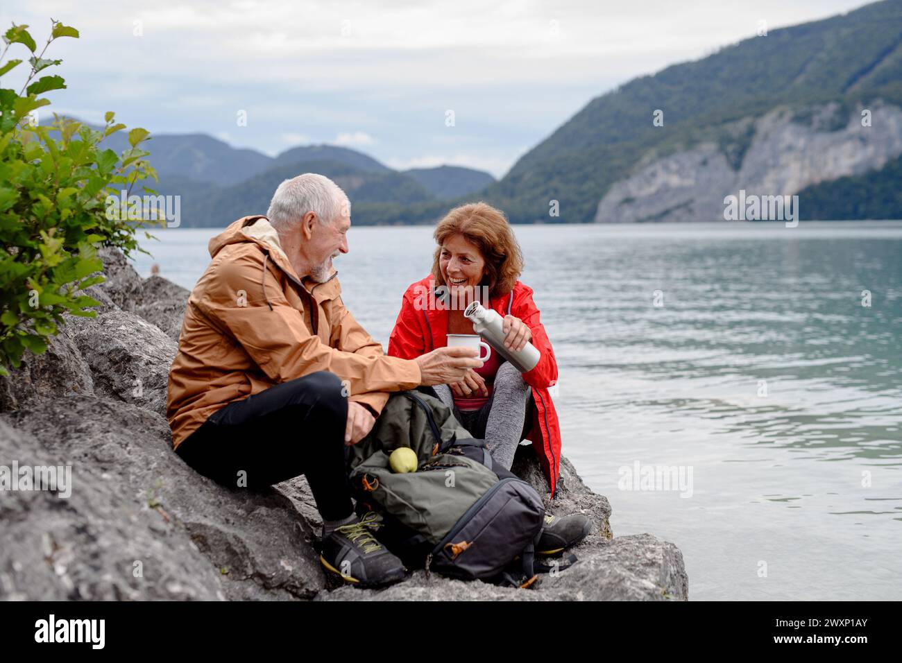 Active elderly couple hiking together in mountains. Drinking coffee and having healthy snack, to ...