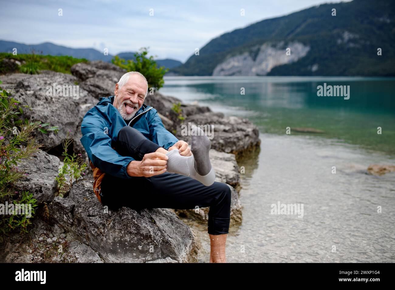Active elderly man putting on sock after barefoot walk in cold water in ...