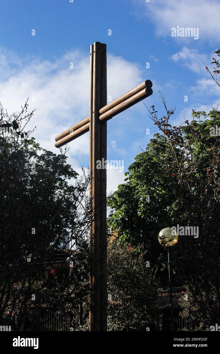 A wooden cross between two trees with green leaves, a lamppost next to ...