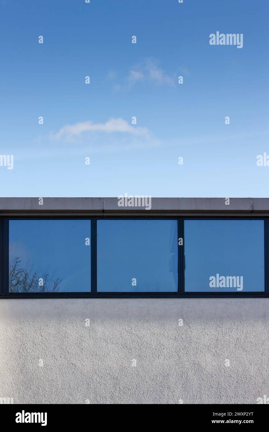 Three windows with black frames reflecting blue sky and white textured ...