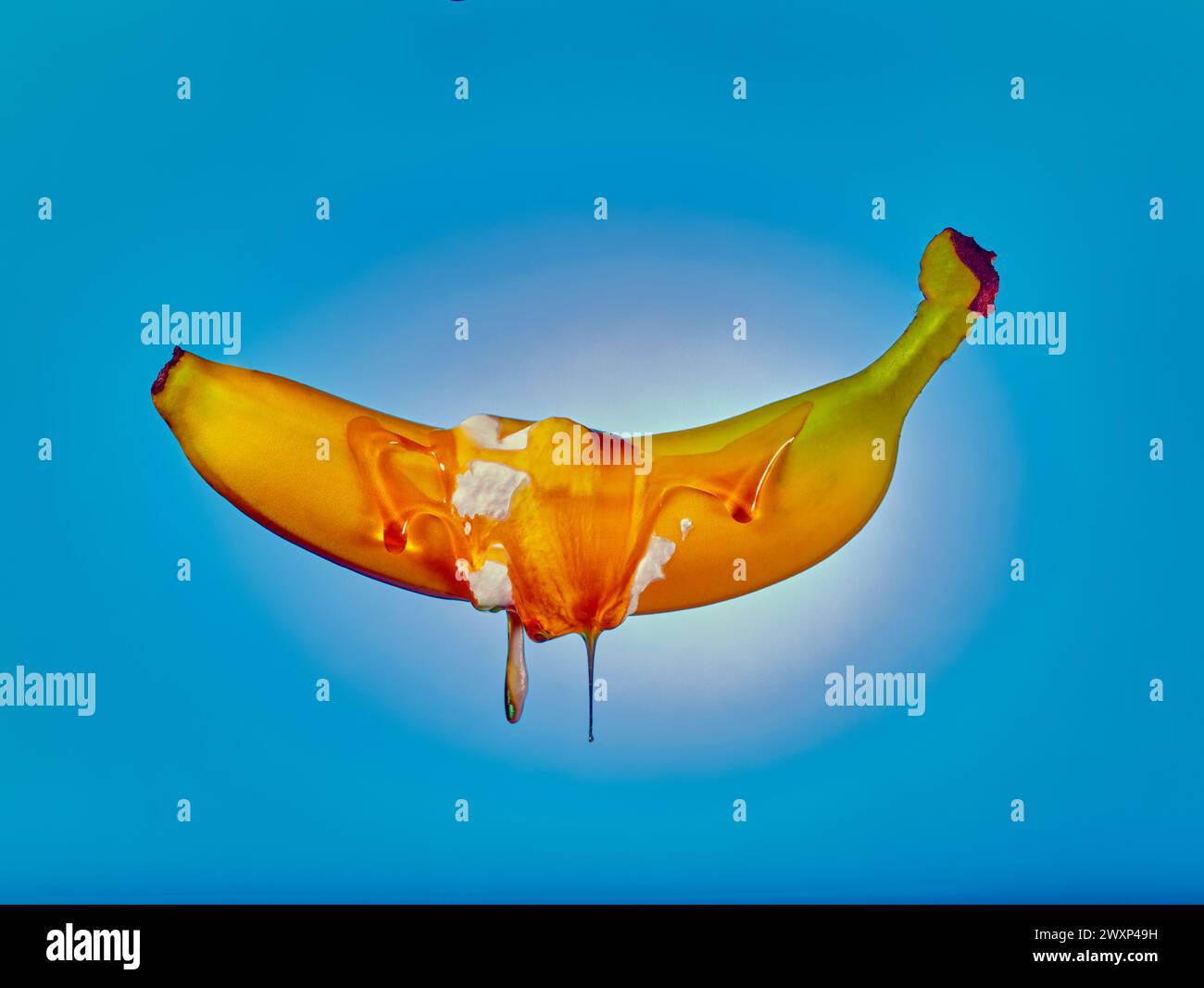 Banana suspended in the air with yogurt and honey dripping from it on a ...