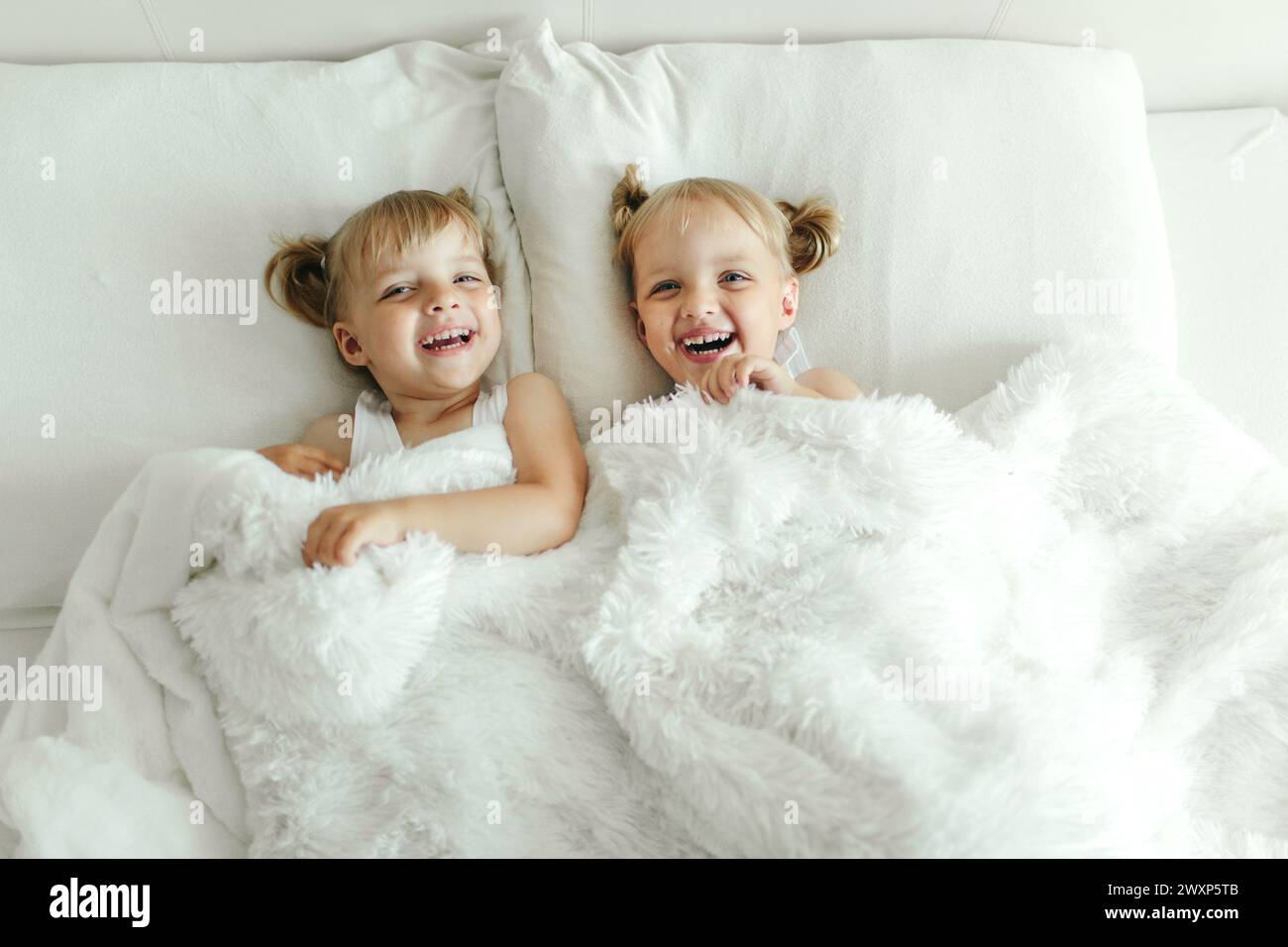 Two young female children are resting comfortably in a bed covered in ...